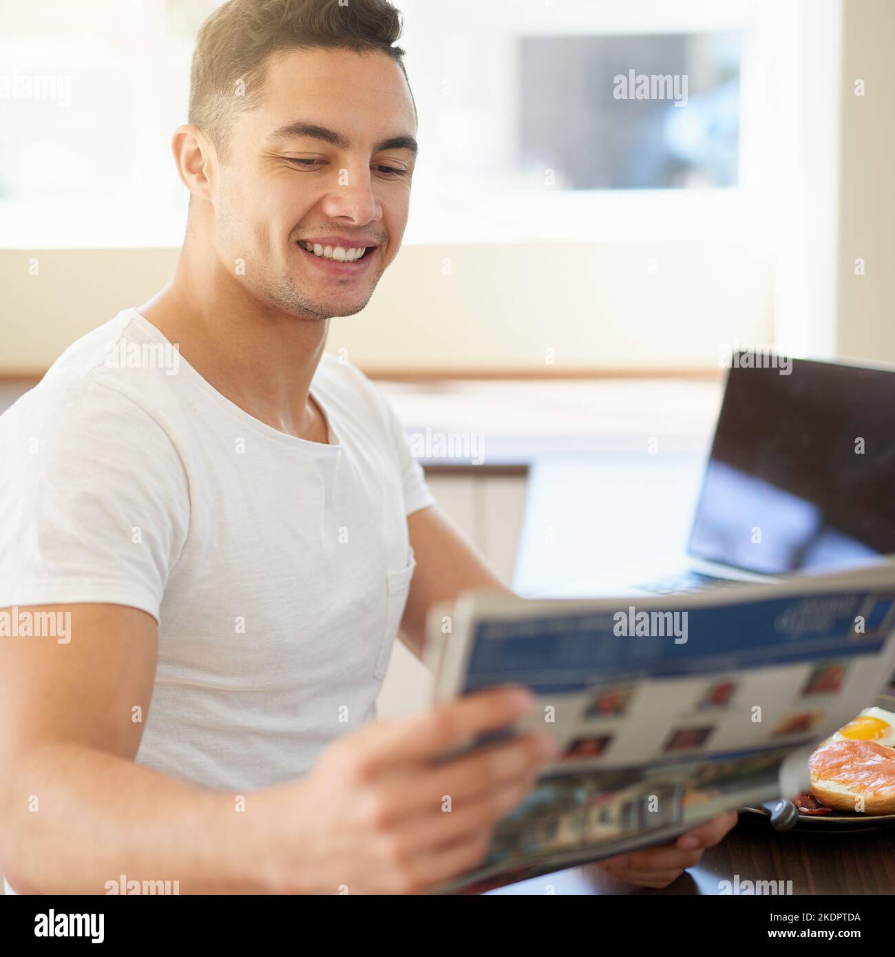 Starting the day on a good note. a young man reading the morning paper ...