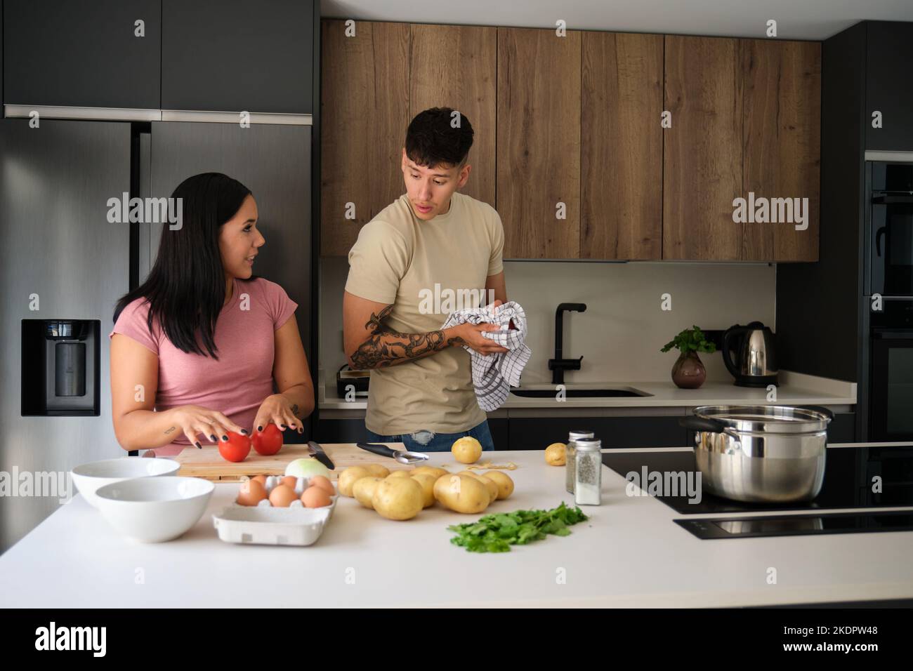 Two young latin people talking about a recipe while cooking together ...