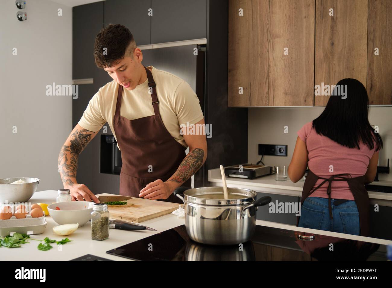 Two young latin people cutting coriander and washing dishes at kitchen ...