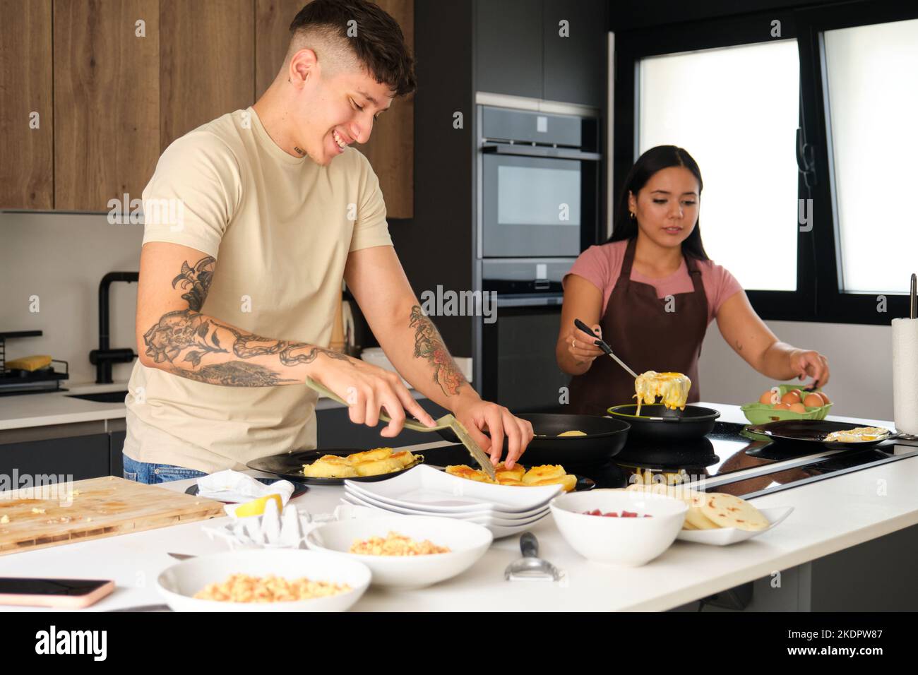 Two young latin people cooking traditional arepas and llapingachos ...