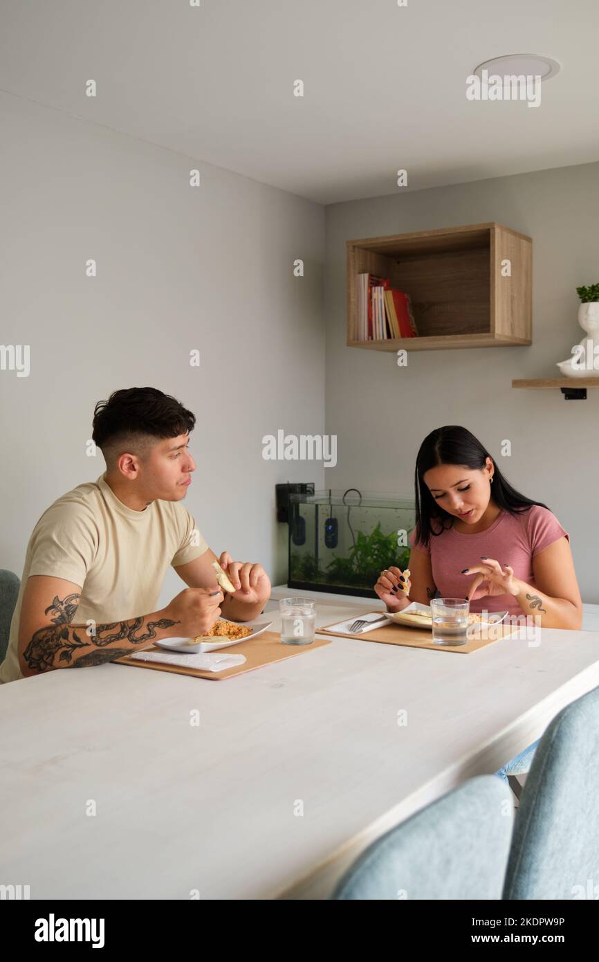Two young latin people eating traditional arepas in the living room ...