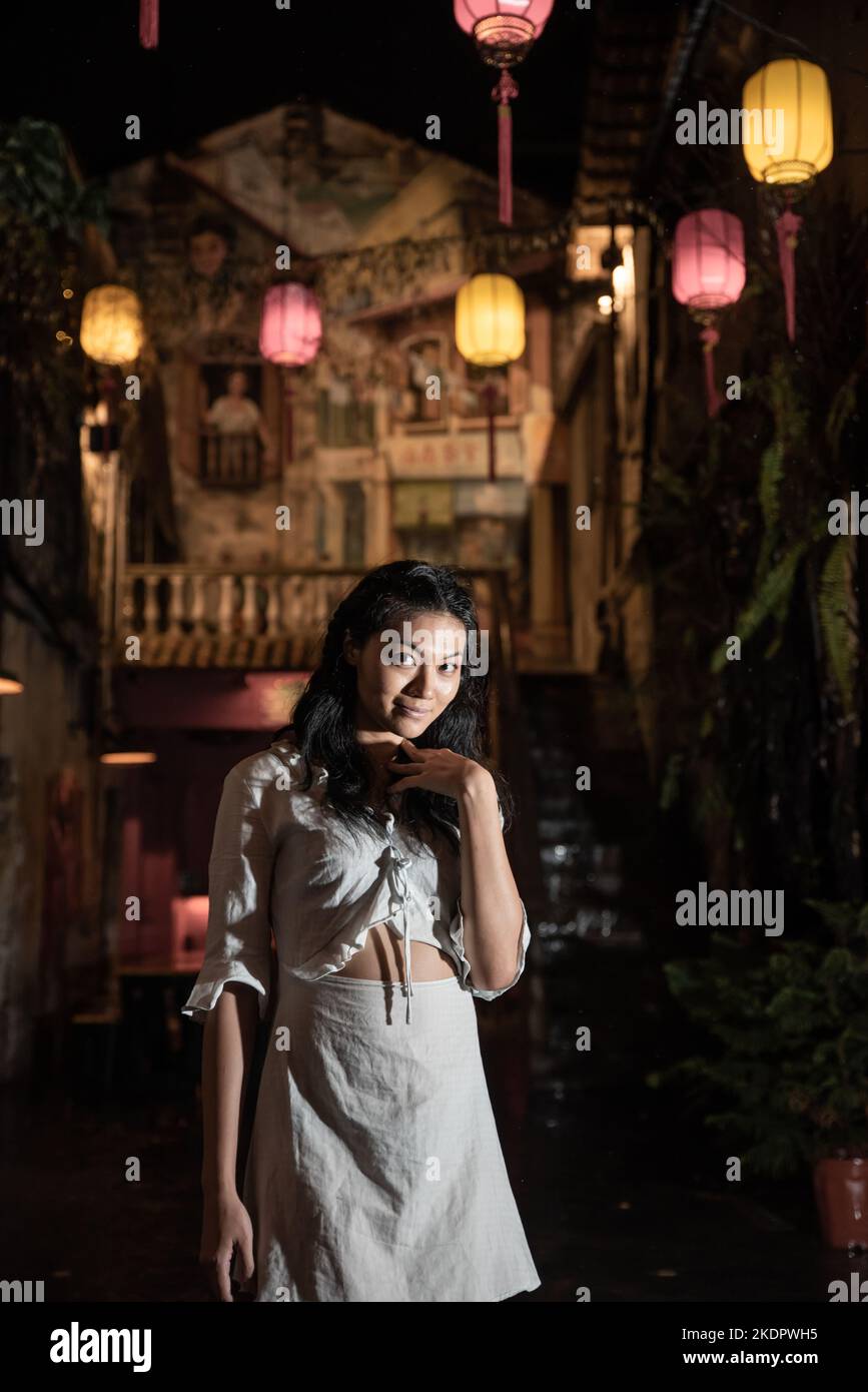 Vertical portrait of a cool asian woman standing in the street at night ...