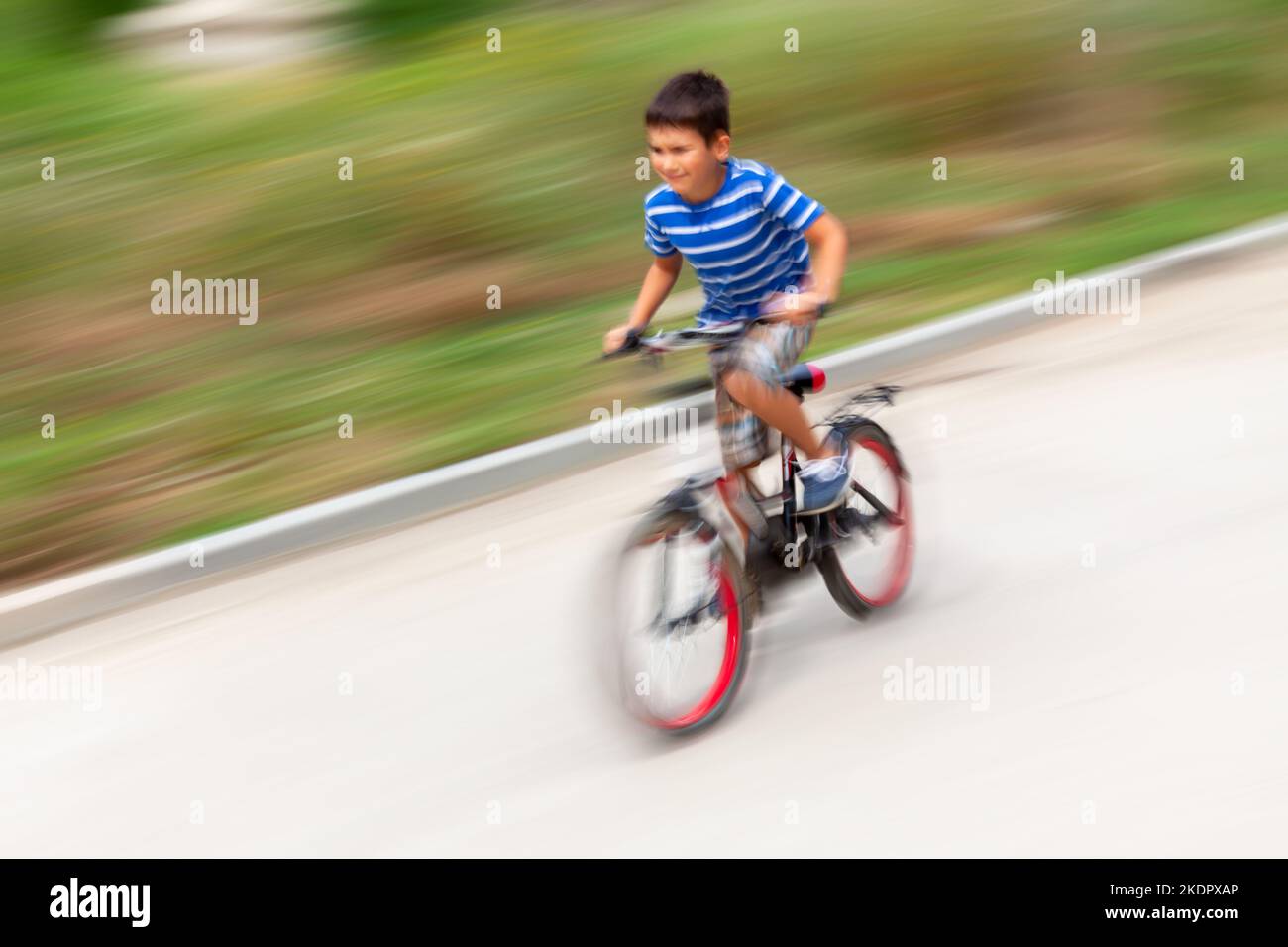 Motion blur image of a boy riding a bike at high speed in a city park ...