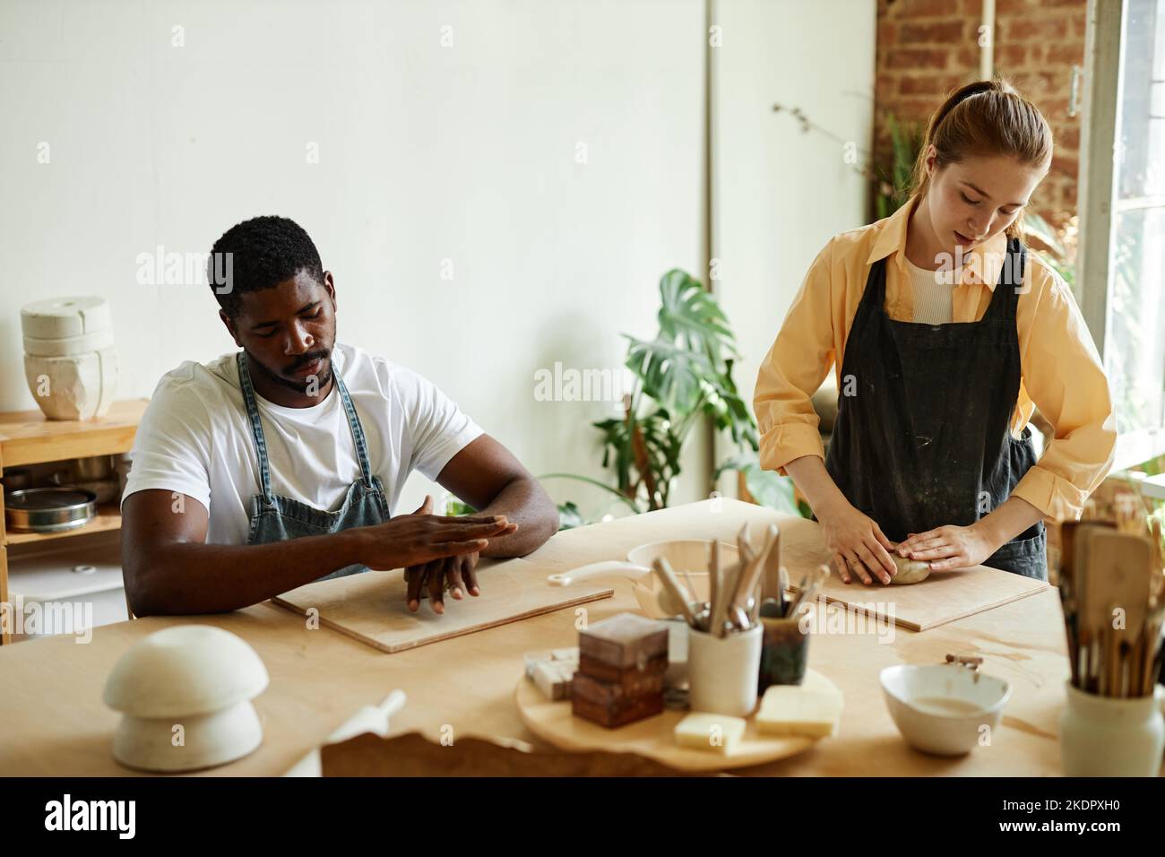 Warm toned portrait of young black man shaping clay while enjoying art ...