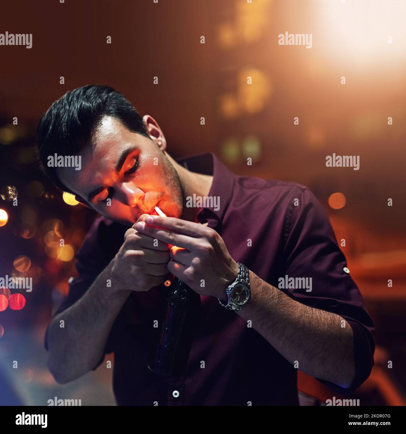 Indulging in one of his vices. a young man lighting a cigarette while ...