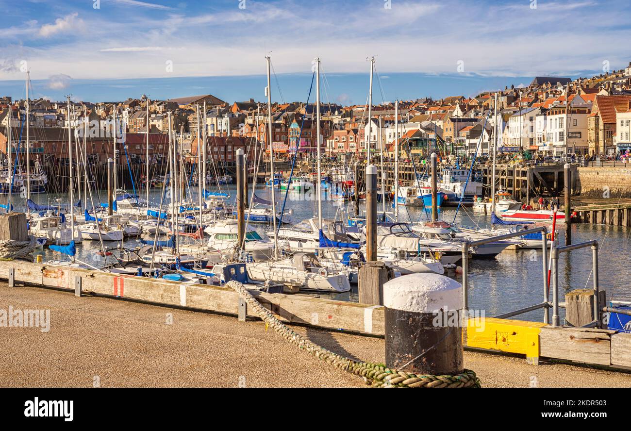A mixture of yachts and fishing boats are in a harbour. The buildings ...
