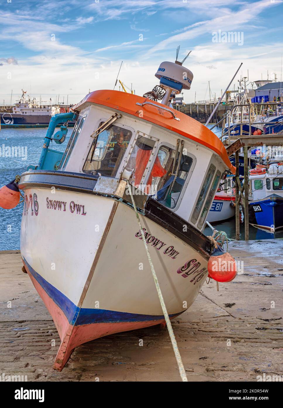 A boat lies to one side aground on a harbour slope. Fishing trawlers ...