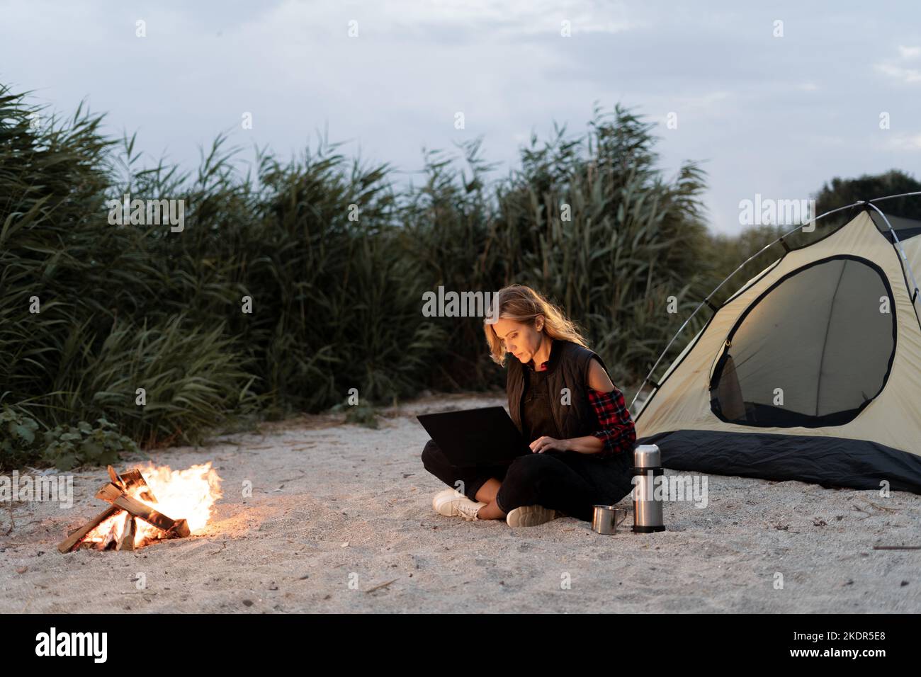 Evening tent camping in seashore. Female traveler uses laptop computer ...