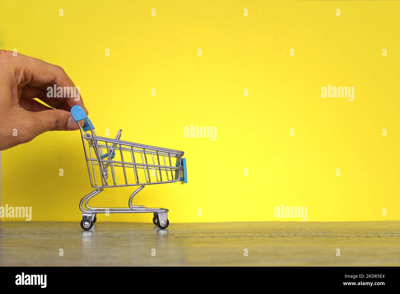 Hand push mini shopping trolley on yellow background with copy space ...