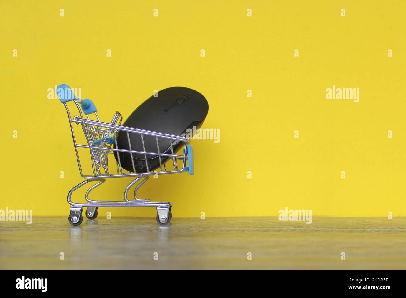 Computer mouse inside shopping trolley on yellow background with copy ...