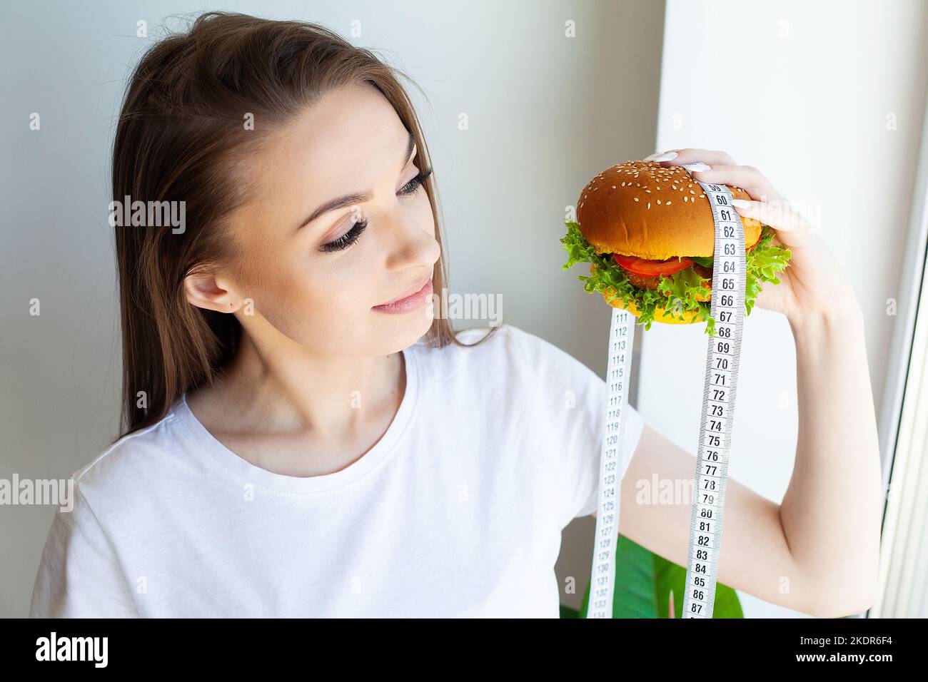 Woman holding harmful fat burger with measuring tape Stock Photo - Alamy