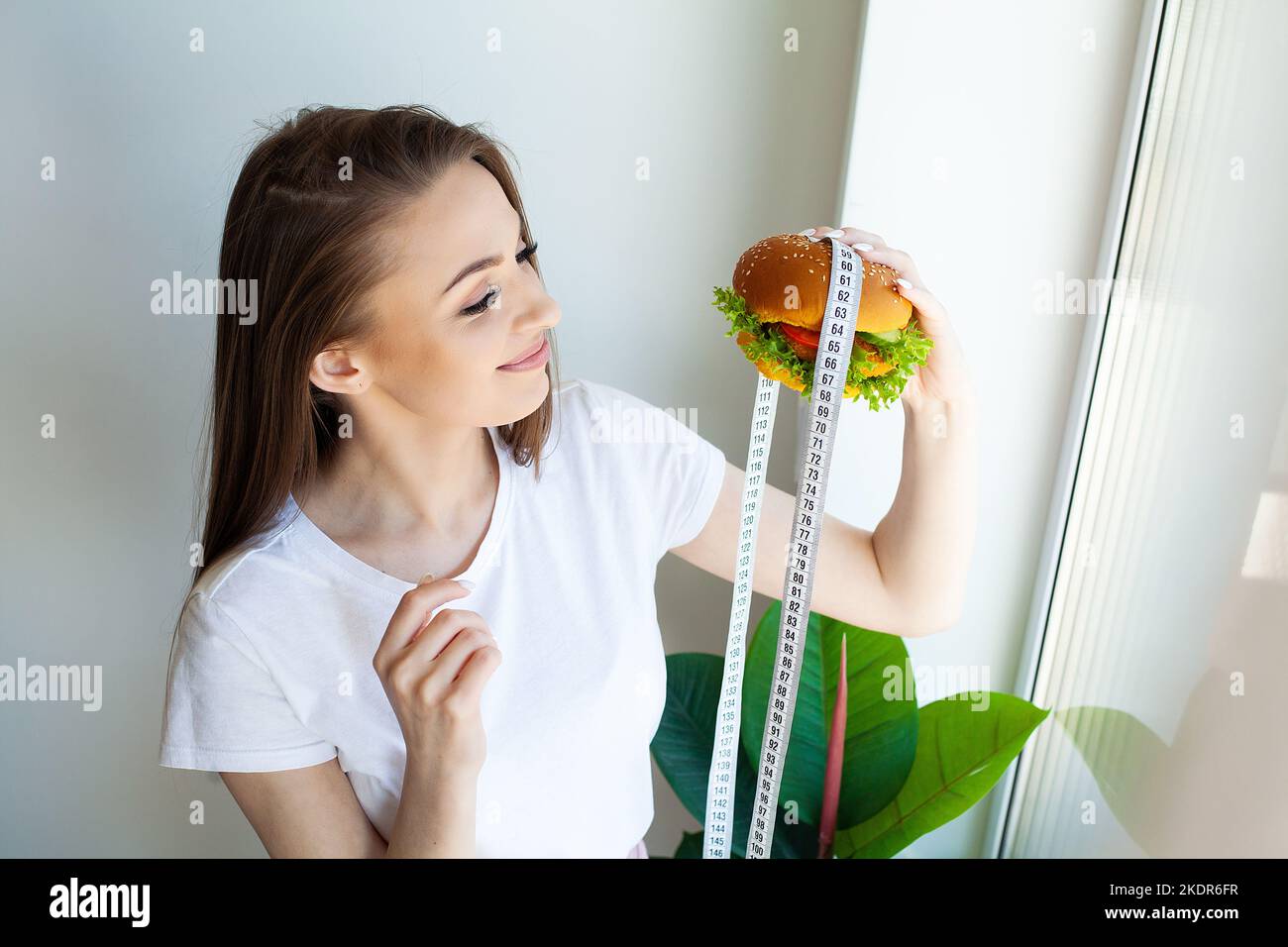 Woman holding harmful fat burger with measuring tape Stock Photo - Alamy