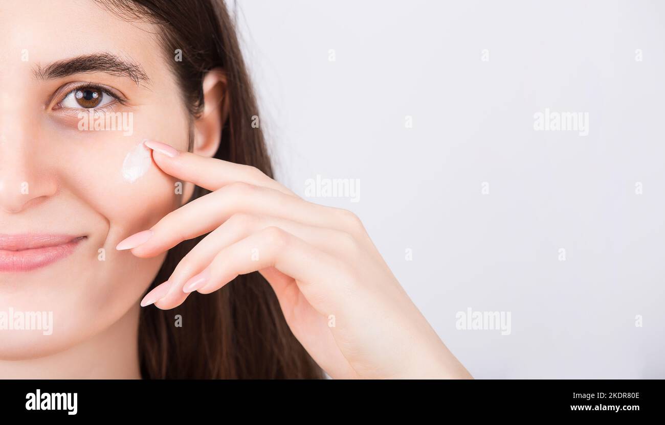Close up young woman applying softening face cream, smiling contented ...