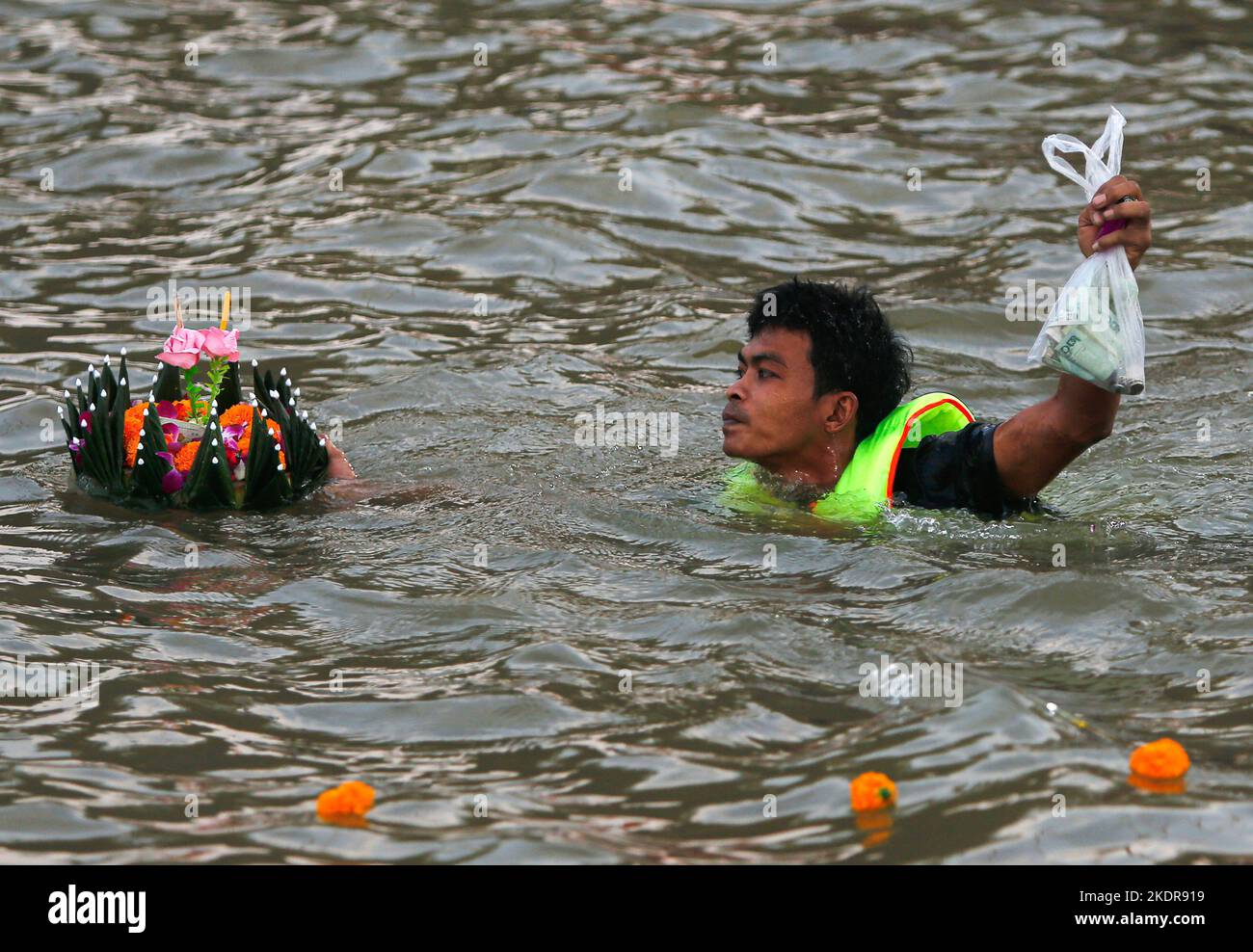 A man carries a Krathong in the Chao Phraya River during the Loy ...