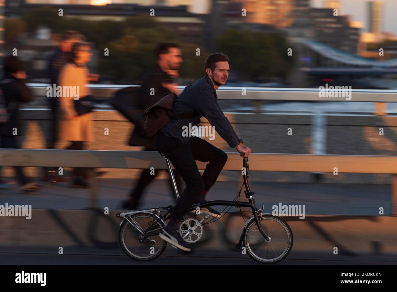 A male commuter riding a Brompton folding bicycle across London Bridge ...