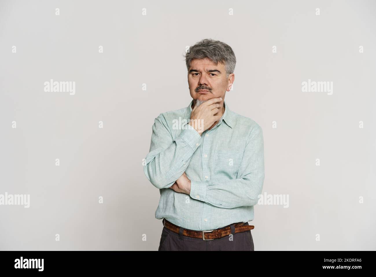 Mature puzzled man with grey beard posing and looking at camera ...
