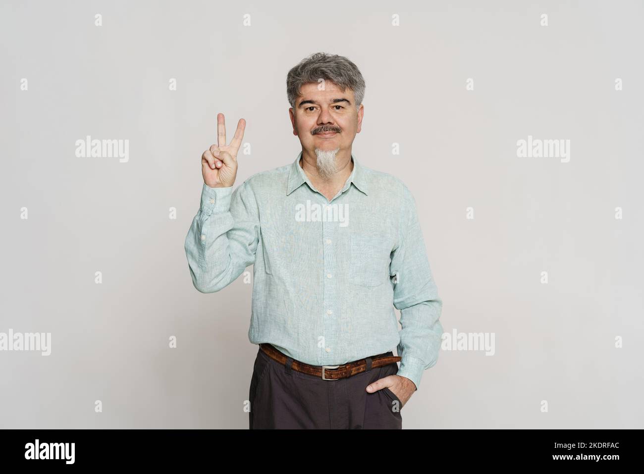 Mature man with grey beard showing peace sign and looking at camera ...