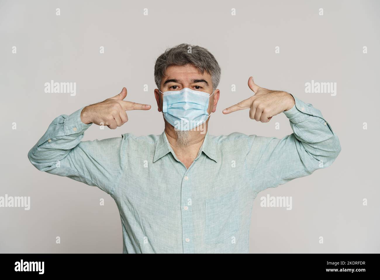 Mature man wearing shirt pointing fingers at his face mask isolated ...