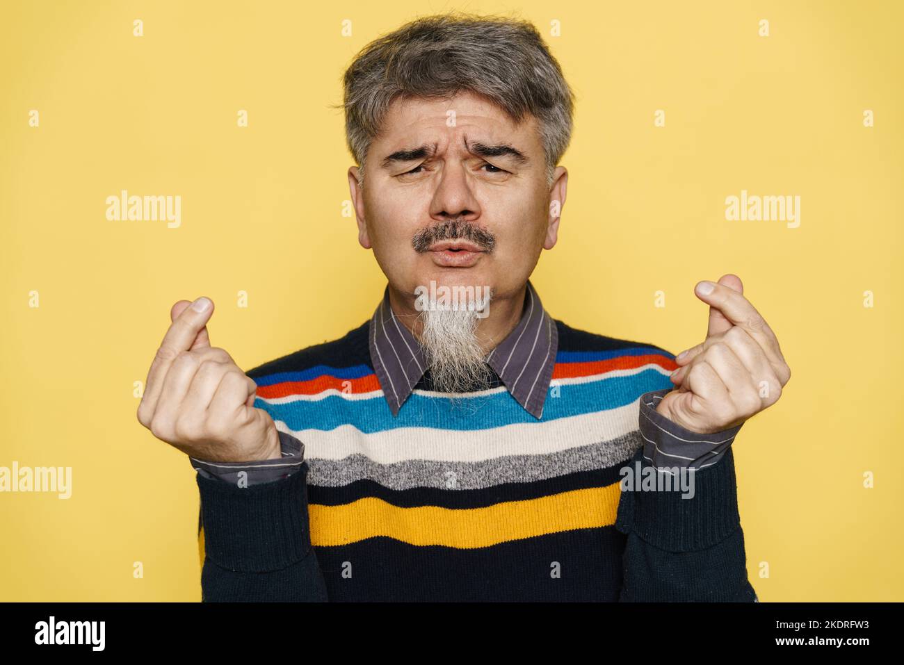 Mature man with grey beard grimacing and rubbing his fingers isolated ...