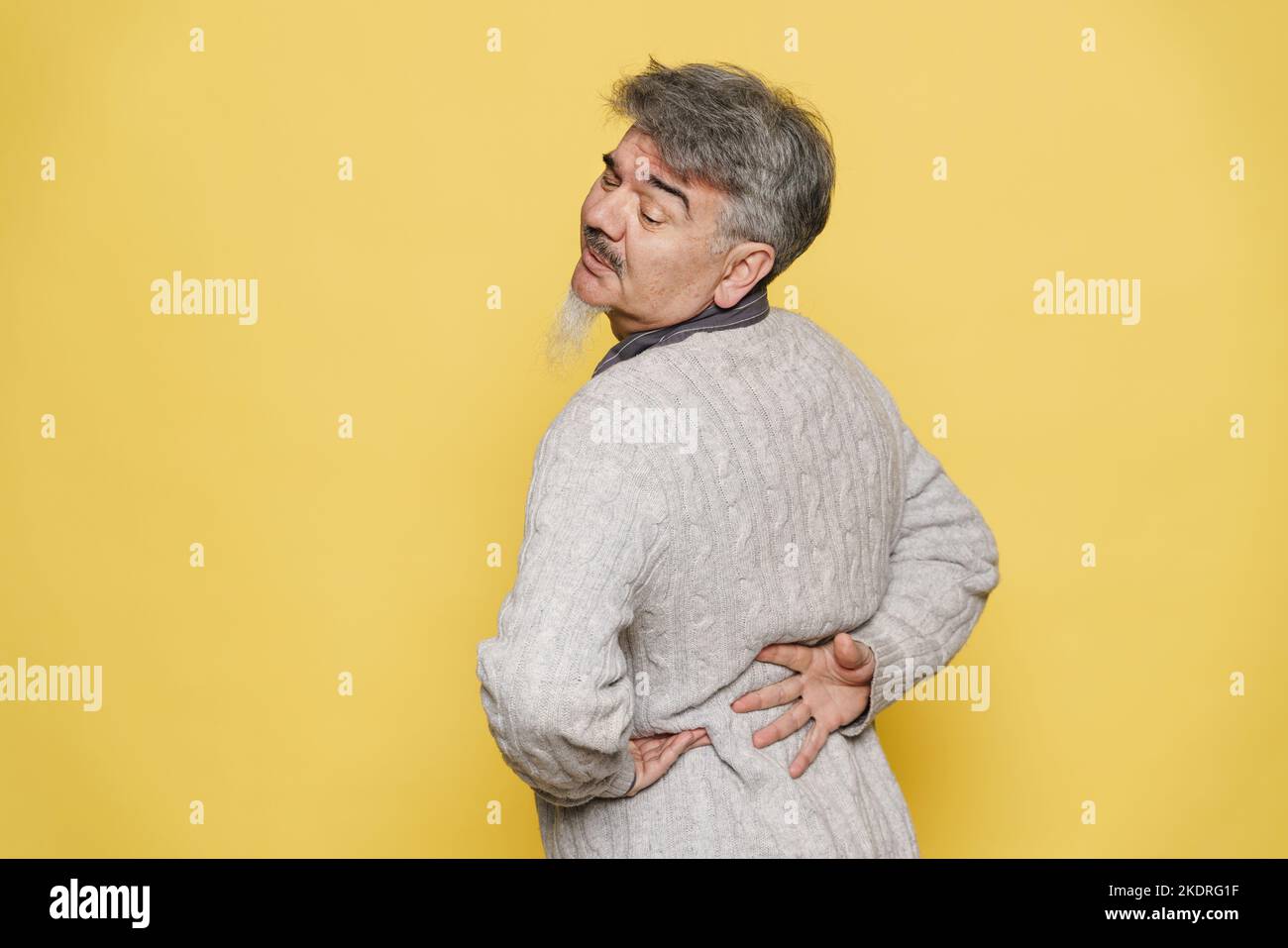 Senior grey man with backache rubbing his back isolated over yellow ...