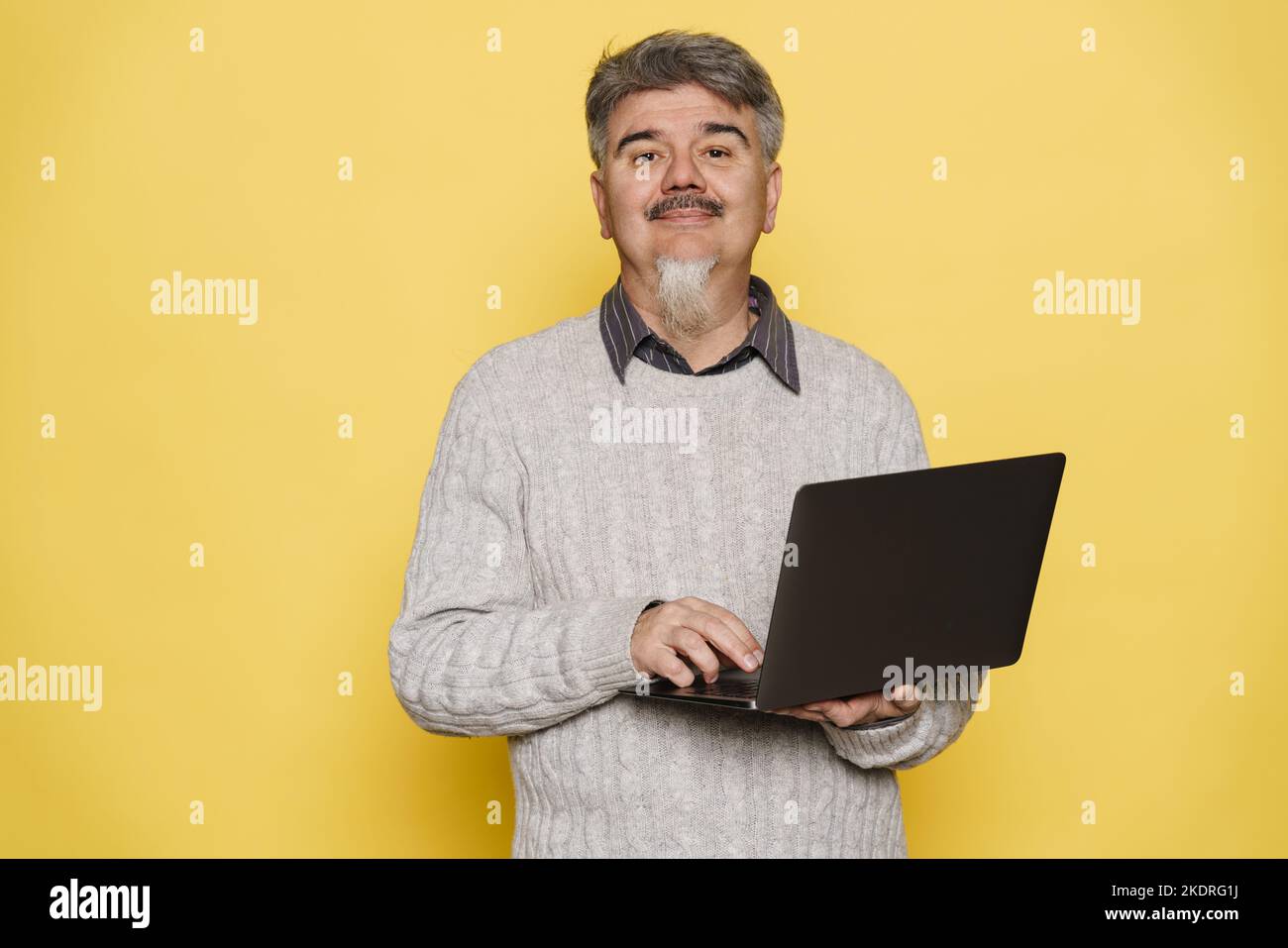 Mature man with grey beard smiling and using laptop isolated over ...