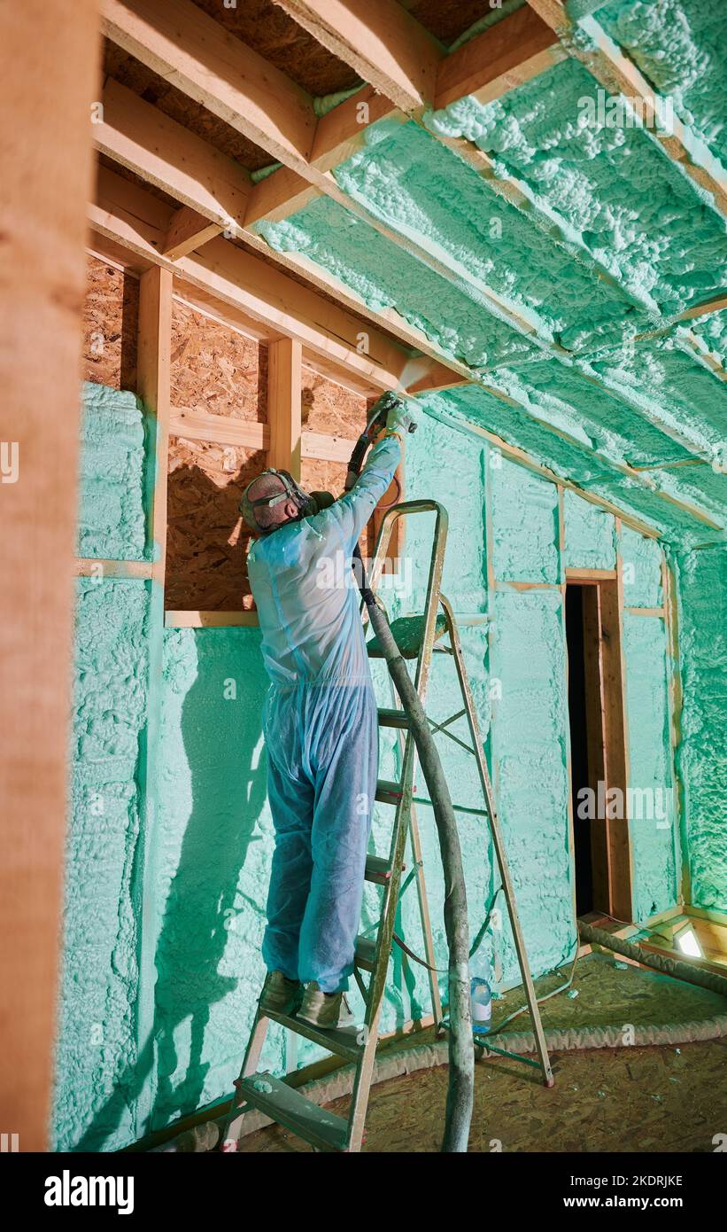 Male builder insulating wooden frame house. Man worker spraying ...