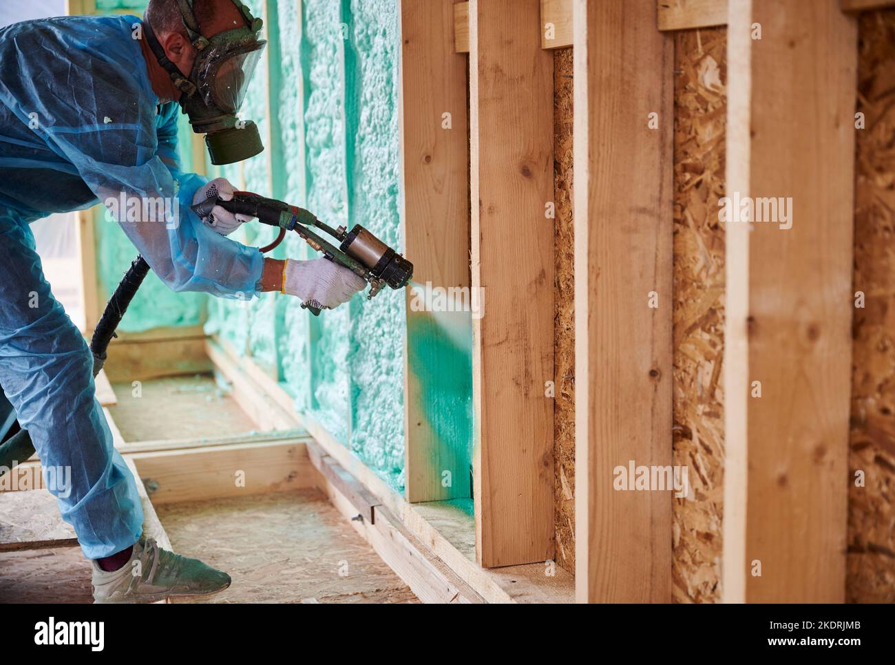 Male builder insulating wooden frame house. Man worker spraying ...