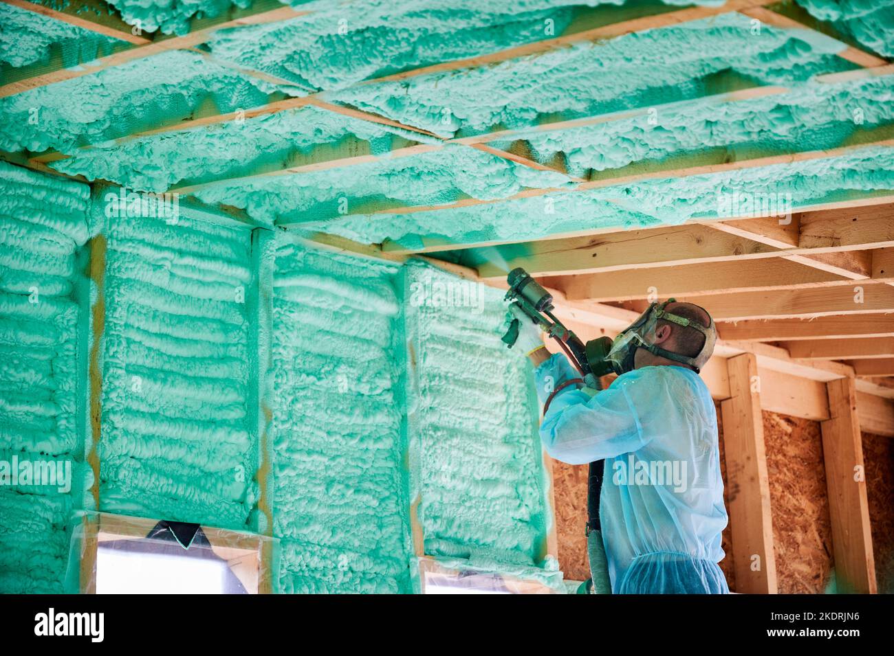 Male builder insulating wooden frame house. Man worker spraying ...