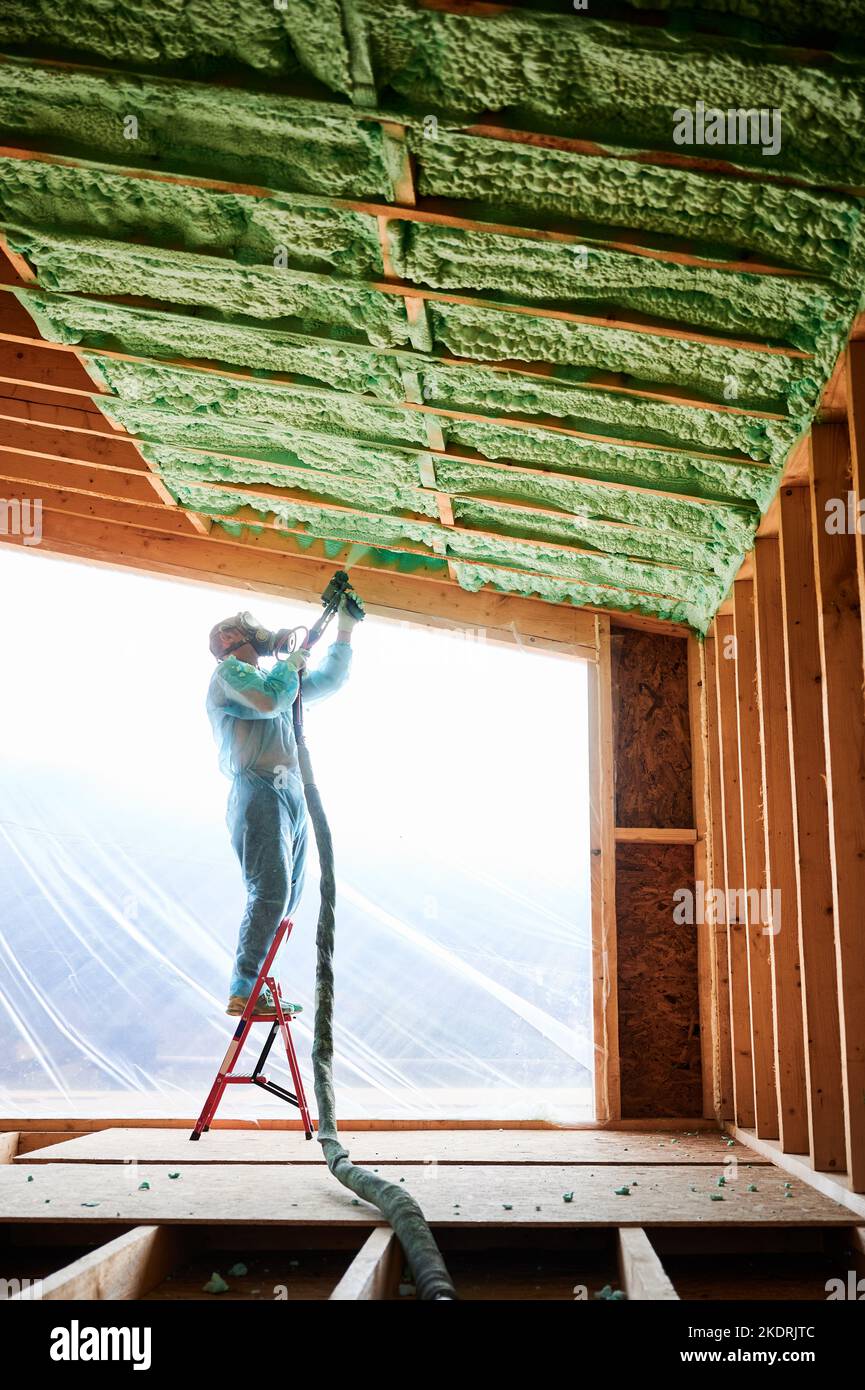 Male builder insulating wooden frame house. Man worker spraying ...