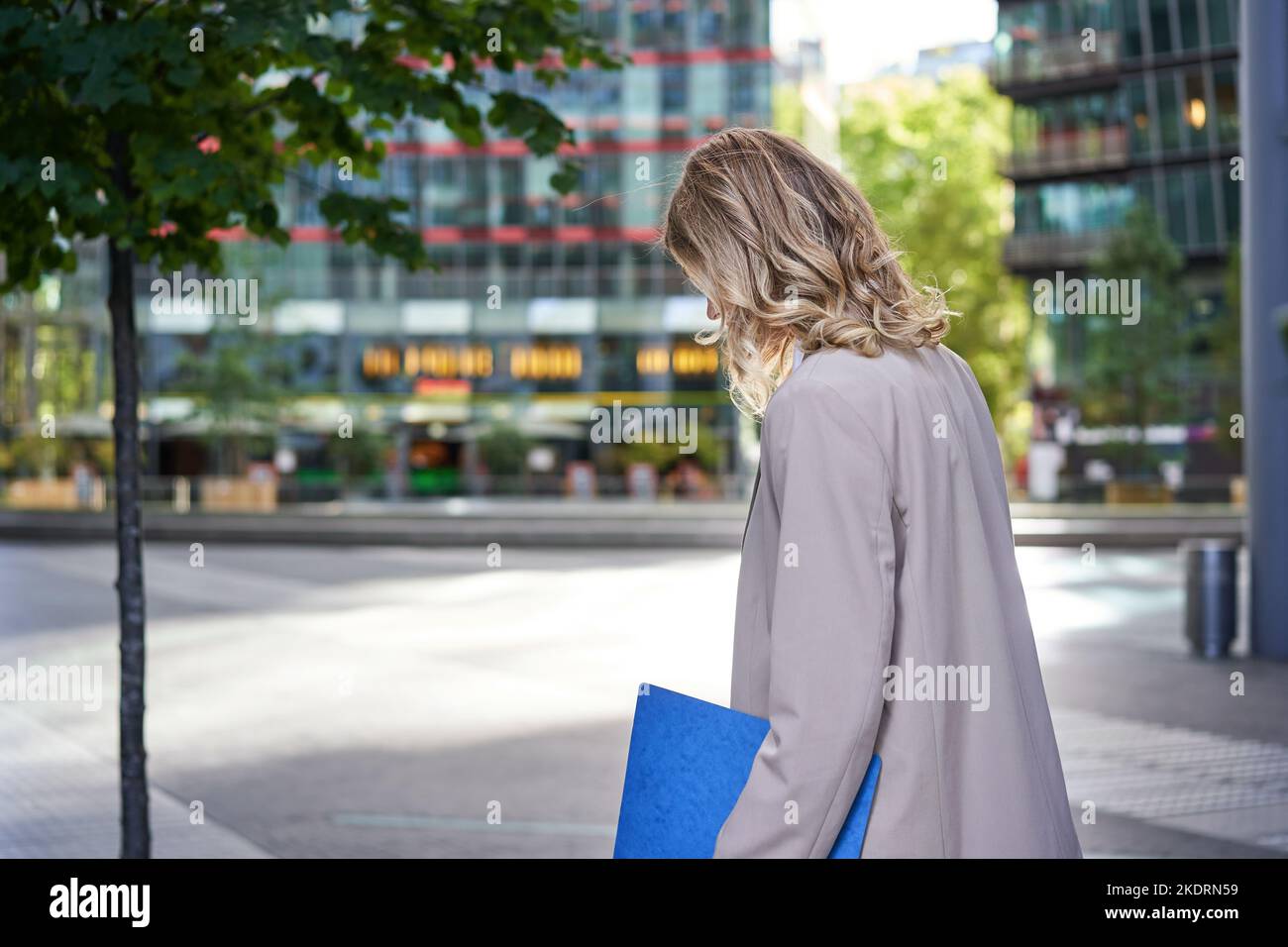 Rear view of young woman in suit, walking on street, holding folder ...