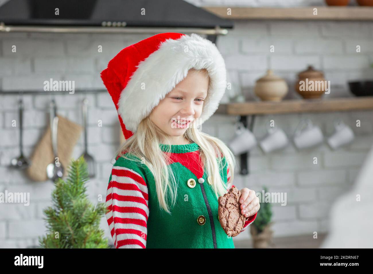 girl in santa claus hat smiling and eating Christmas cookie Stock Photo ...