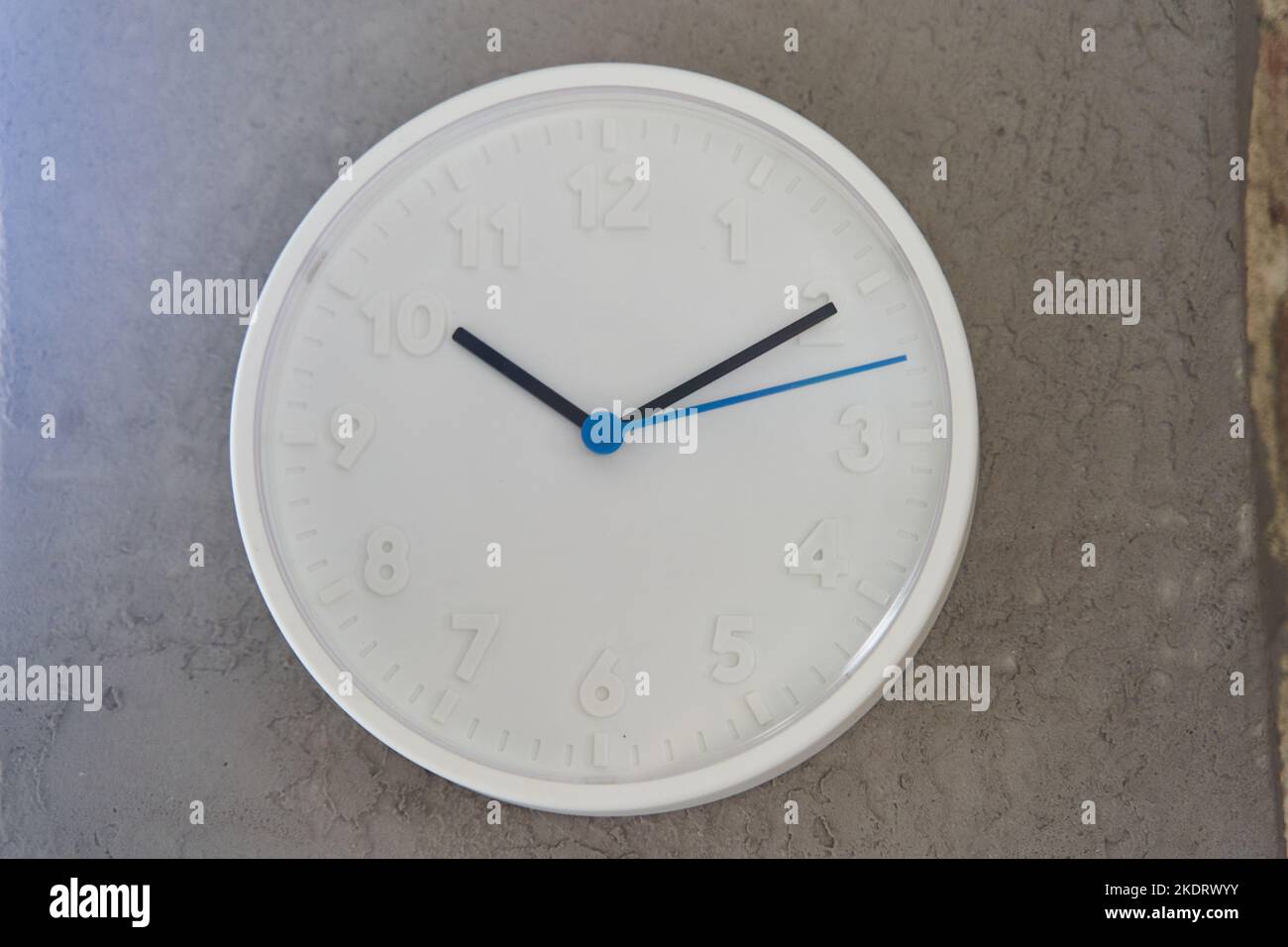 White big wall clock with blue second hand on rough cement wall Stock ...