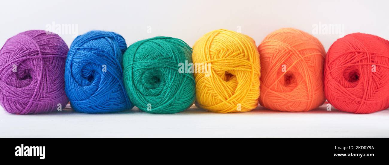 Many multi-colored balls of threads on knitted fabric on white wooden ...