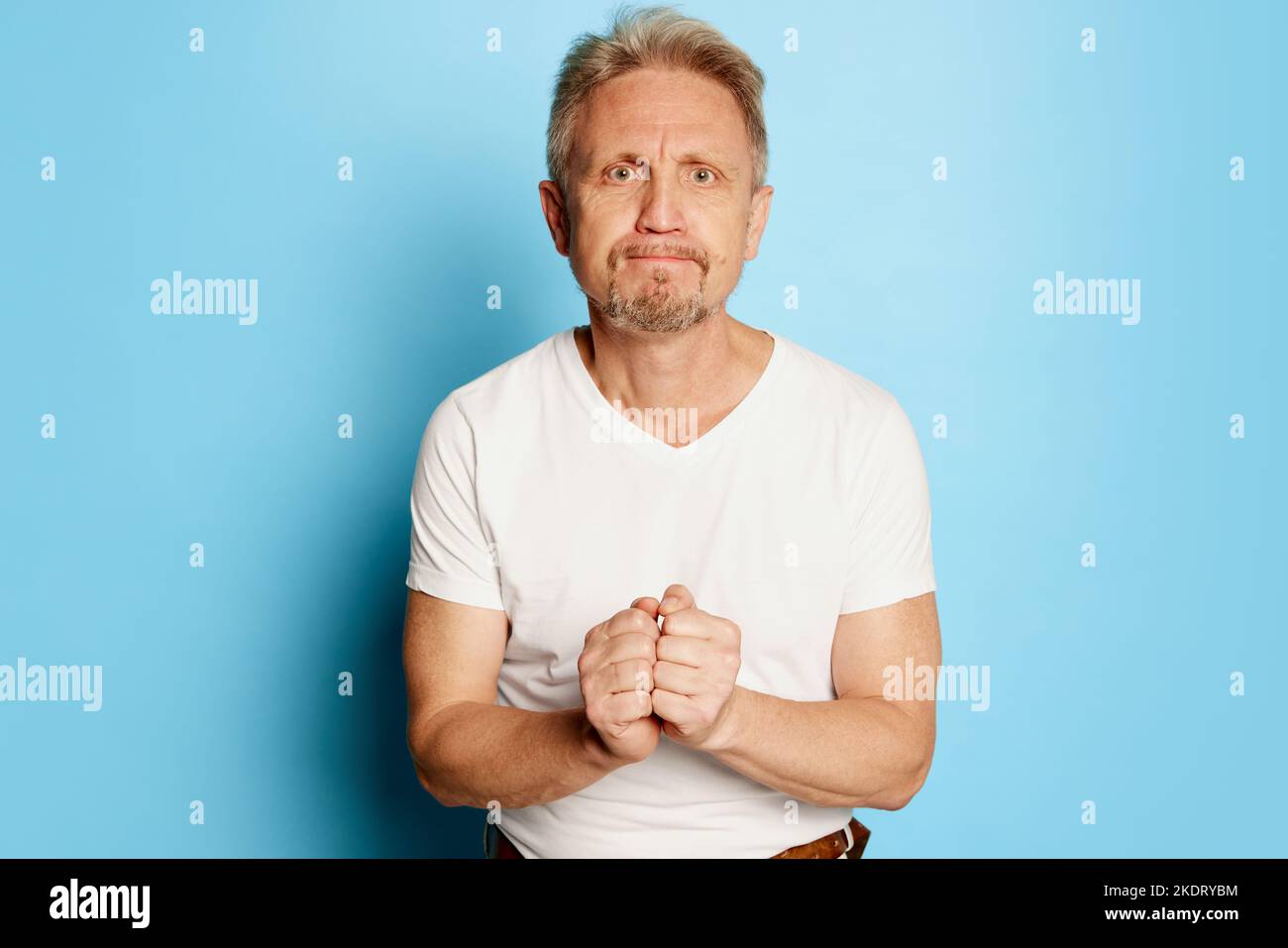 Portrait of mature man in white T-shirt posing isolated over blue ...