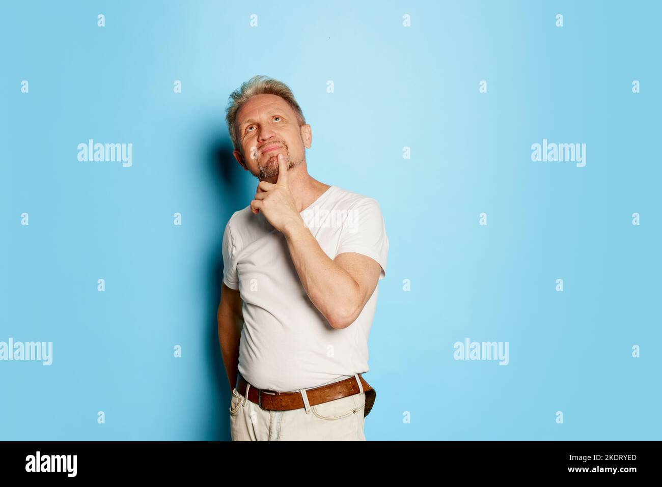 Portrait of mature man in white T-shirt posing isolated over blue ...