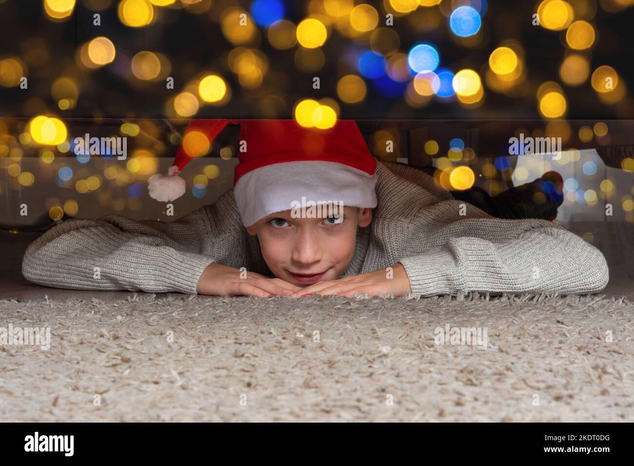 A pretty teenage boy in a Santa hat lying on the floor under the bed ...