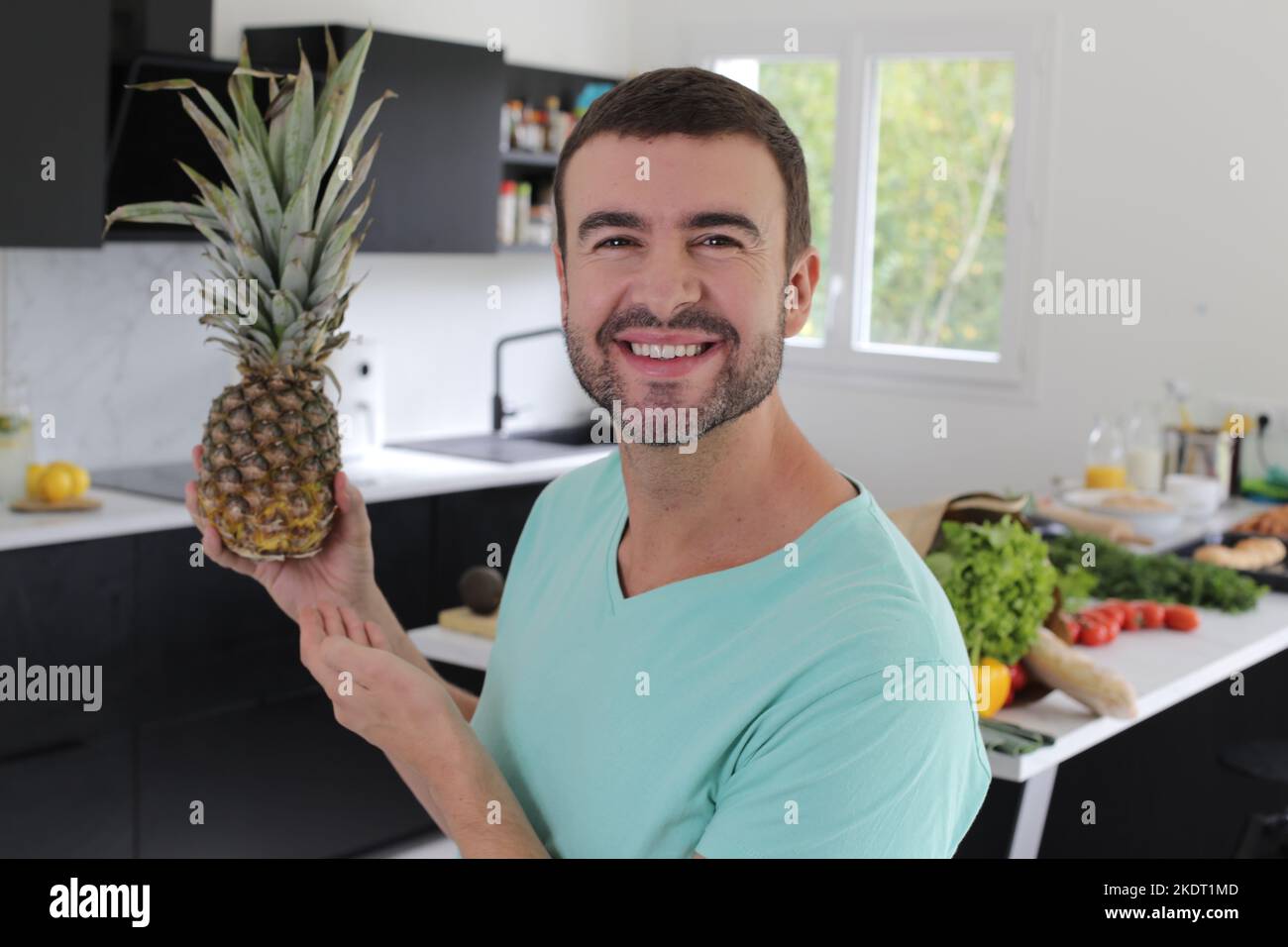 Man holding a whole pineapple in the kitchen Stock Photo - Alamy