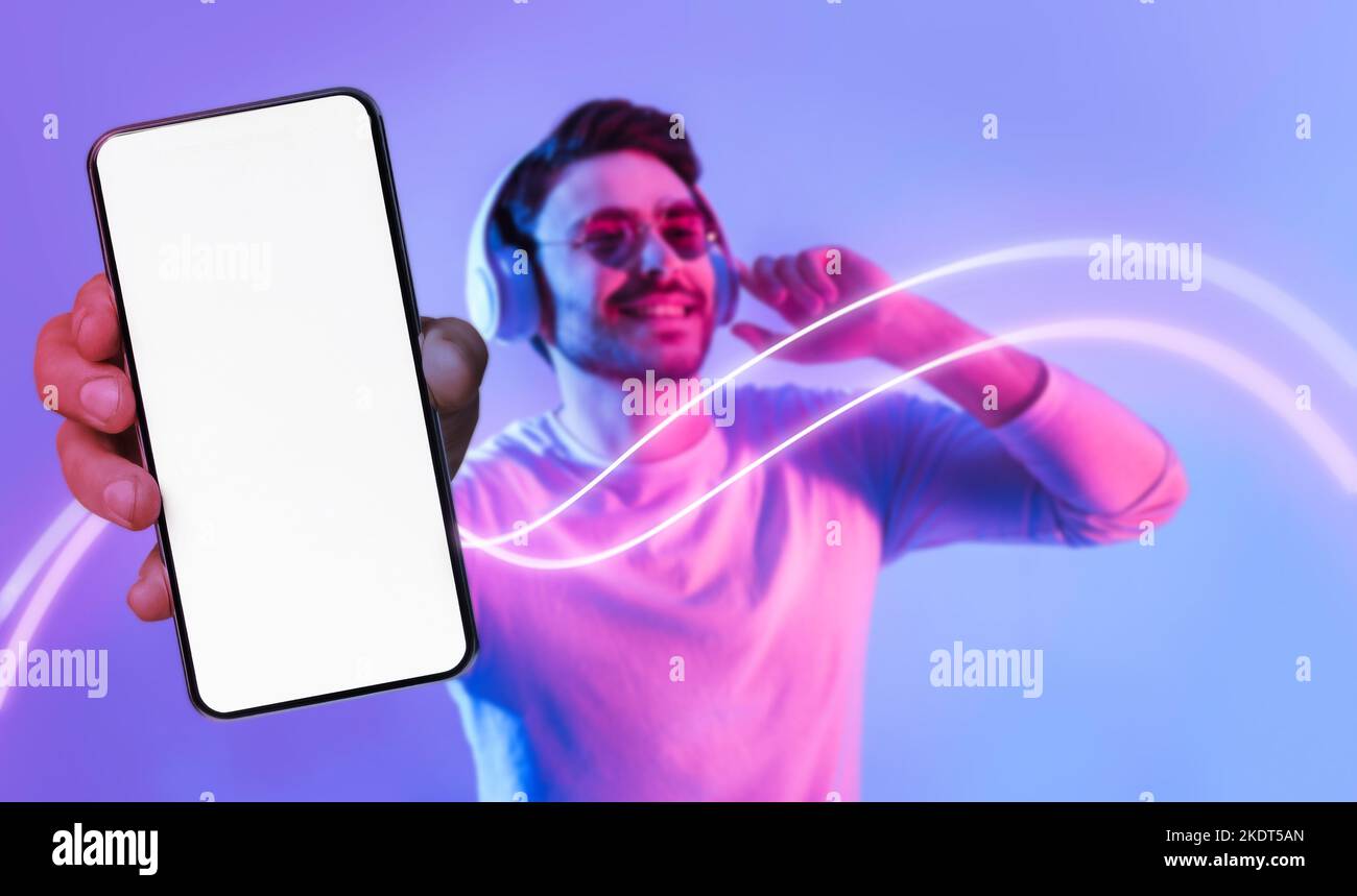 Positive young man showing cell phone, using wireless headphones Stock ...