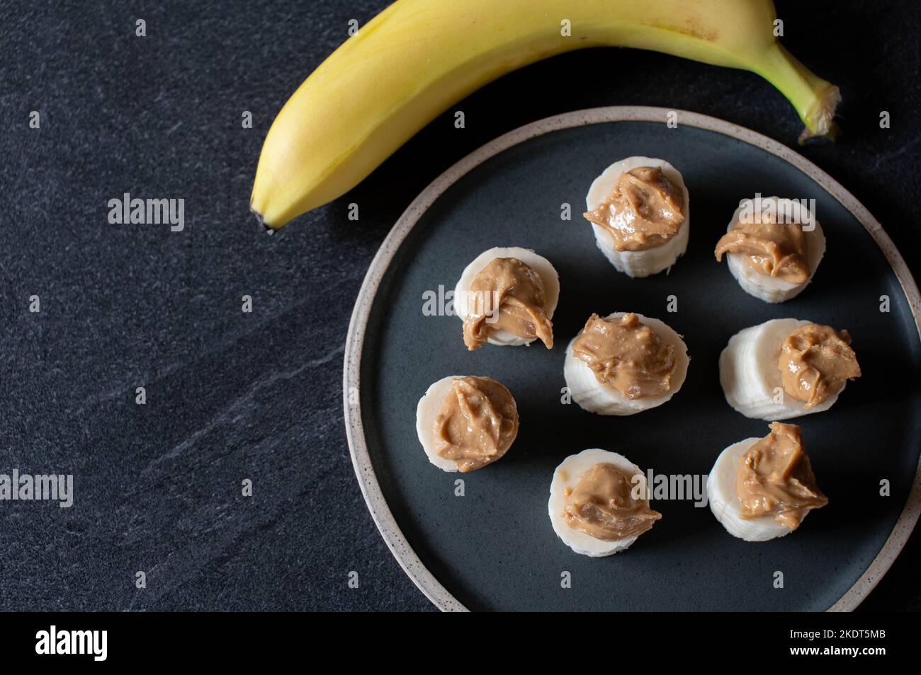 Healthy snack with sliced banana and crunchy peanut butter on dark ...