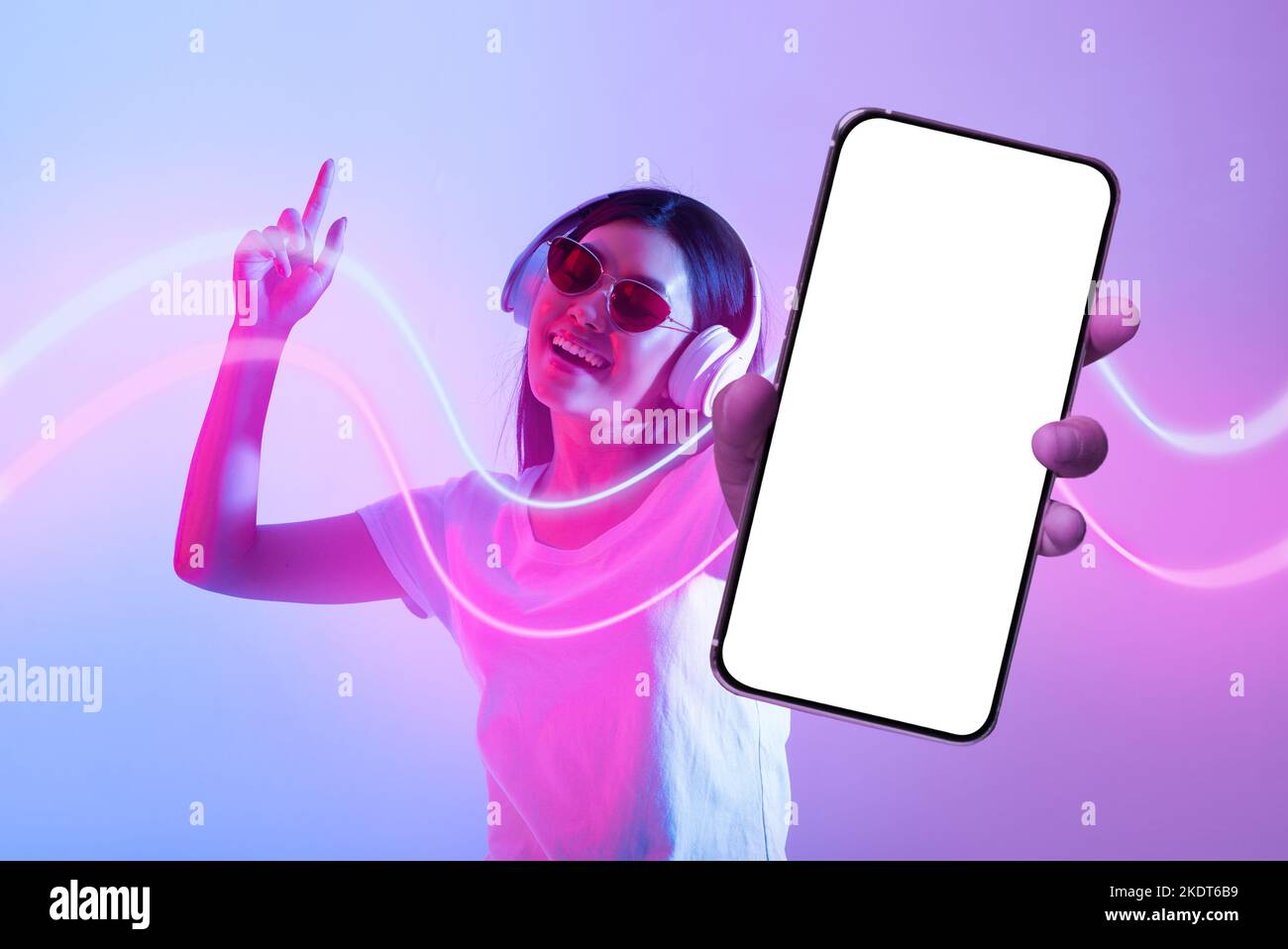 Joyful asian woman showing cell phone, using wireless headphones ...