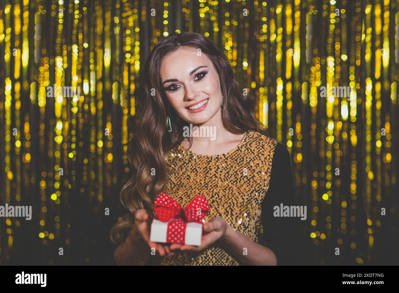 Beautiful woman holding gift on golden bokeh background Stock Photo - Alamy