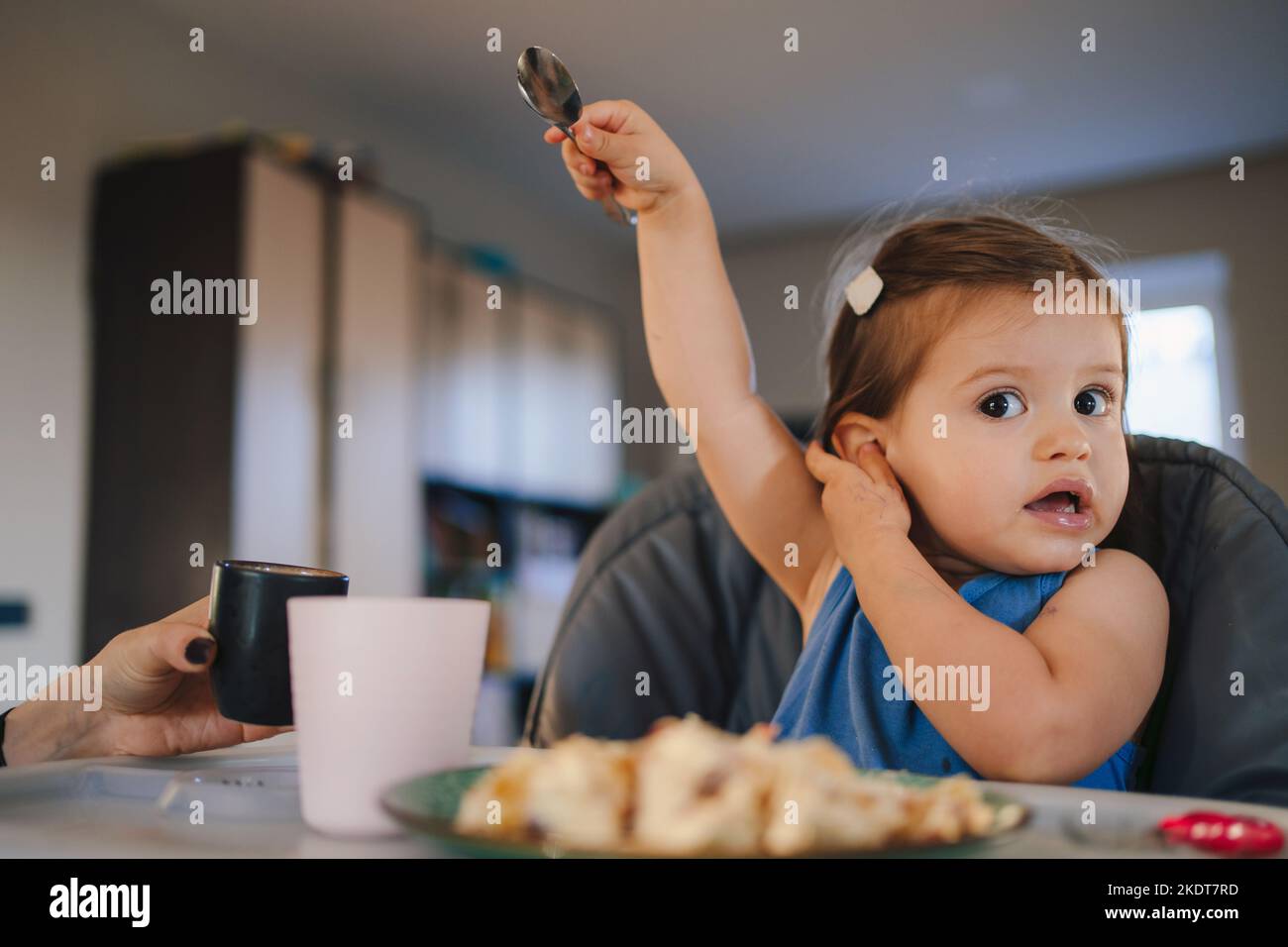 Cute little baby having lunch, sitting at table in high chair holding ...