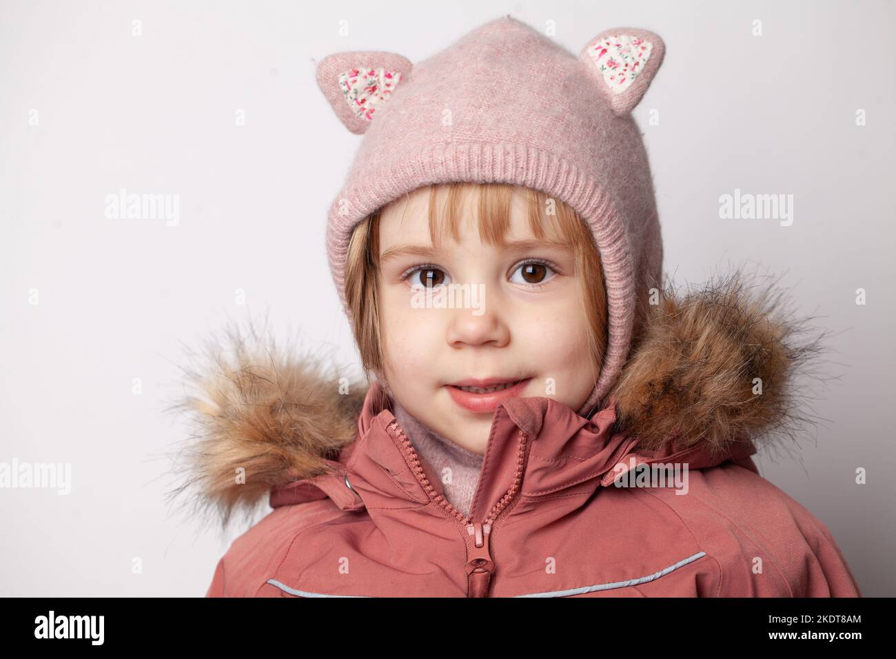 Portrait of cute little girl in pink coat and hat on white studio wall ...