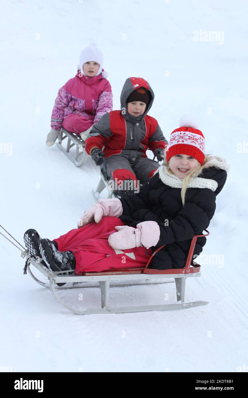 Kids in winter coats in the snow park riding on the sleds Stock Photo ...