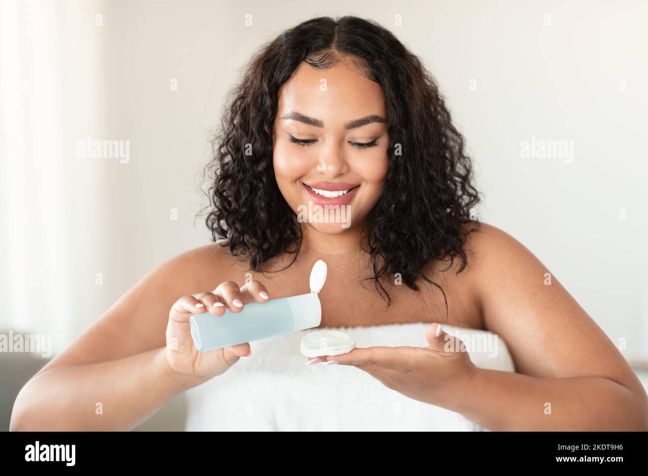Attractive black body positive woman using cotton pads and micellar ...