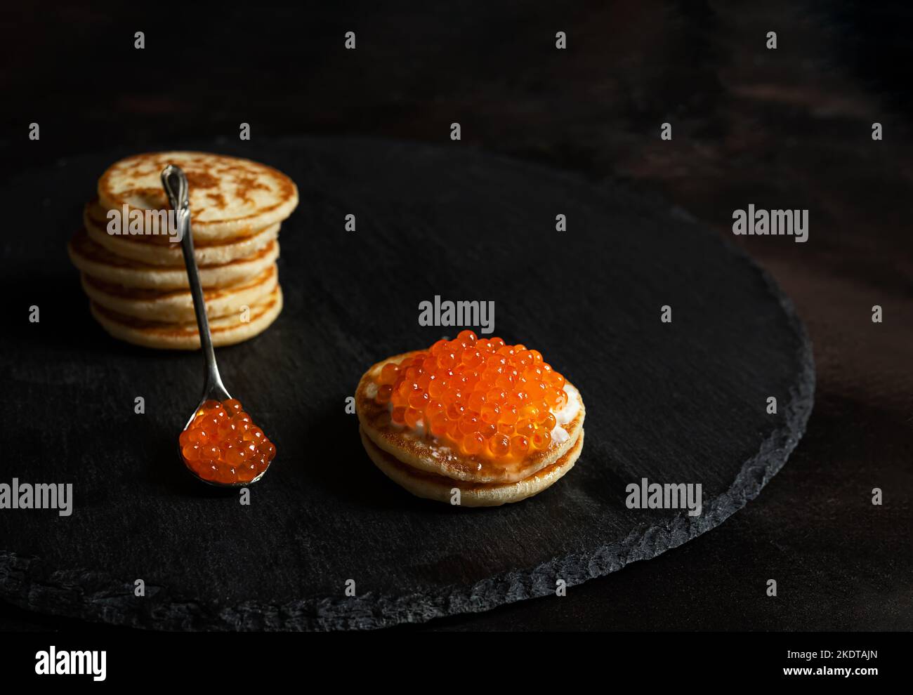 Red caviar in a spoon and on small pancakes blinis with sour cream on a ...