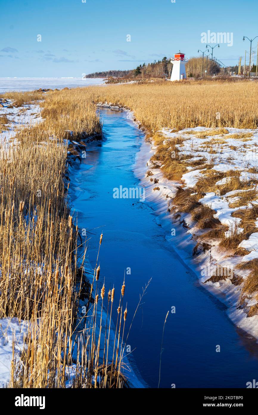 A stream running out to sea through a salt marsh with a lighthouse in ...