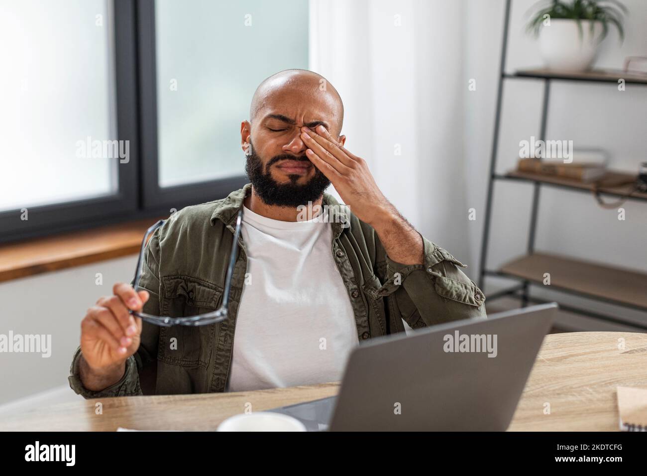 Tired mature male freelancer rubbing irritated eyes, sitting at desk ...