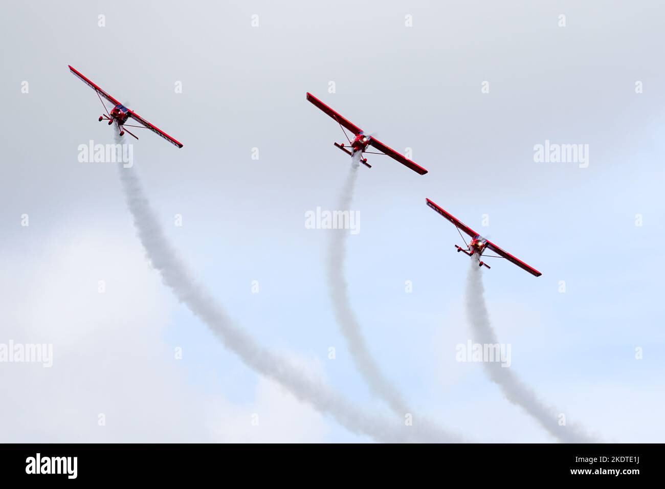 Three small red sports planes with smoke stripes make a parallel flight ...