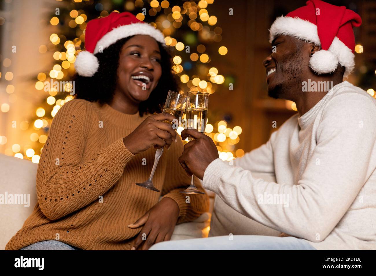 Cheerful millennial black lady and man in Santa hats, cheers with ...
